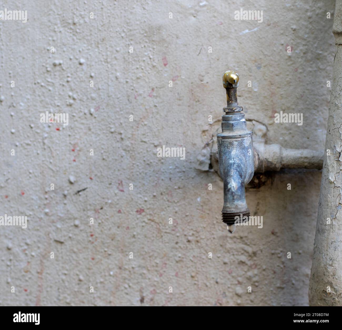A tap mounted on an old wall with a small drop of water coming from it ...