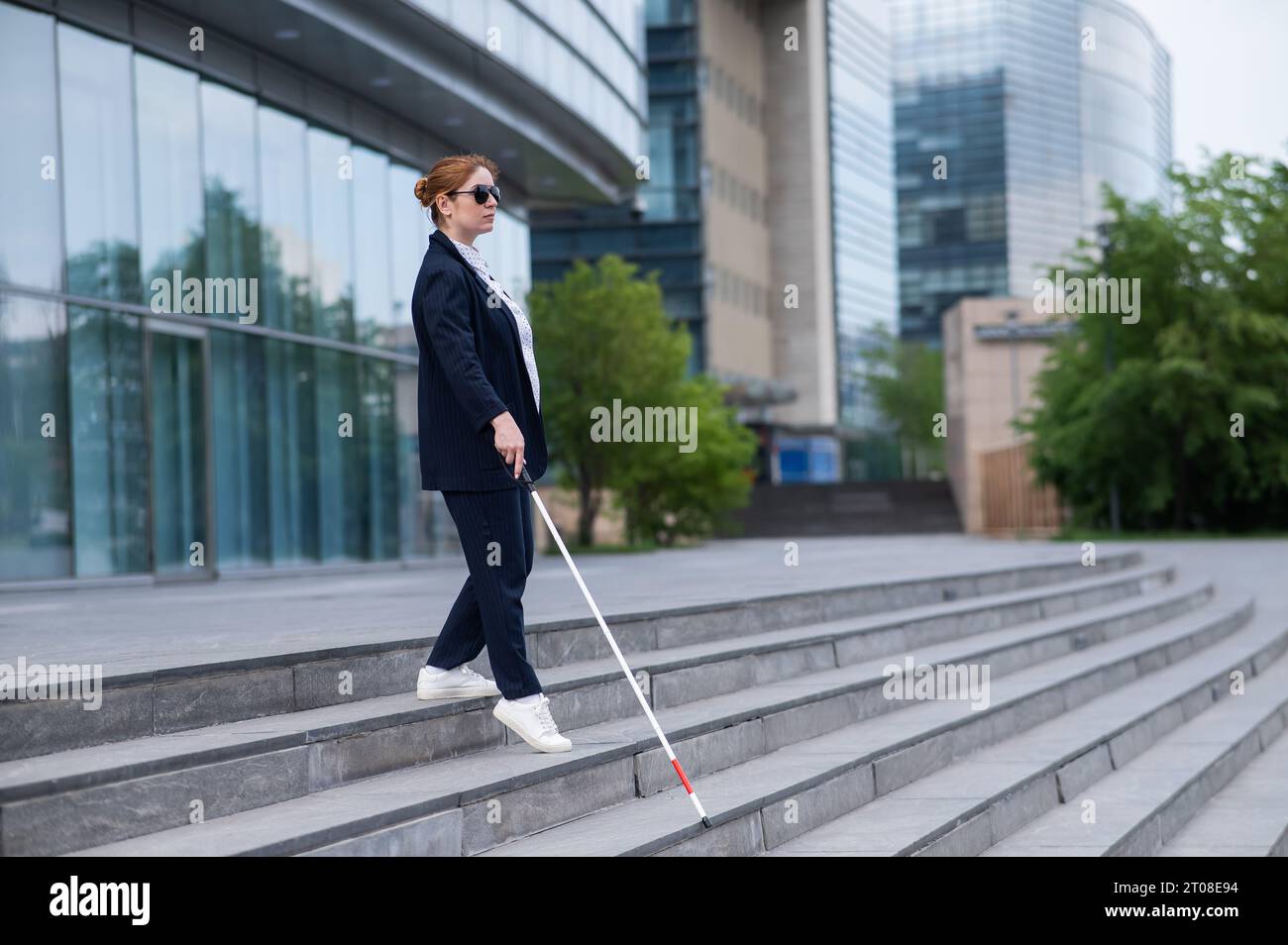 Blind business woman descending stairs with a tactile cane from a ...