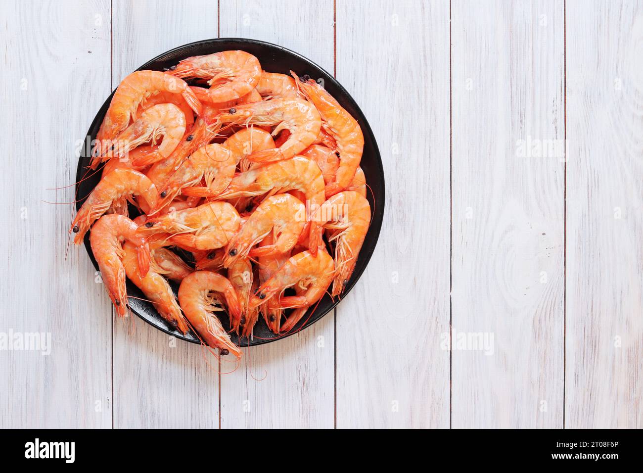 Boiled shrimp in a black plate on a light wooden background. Fresh ...