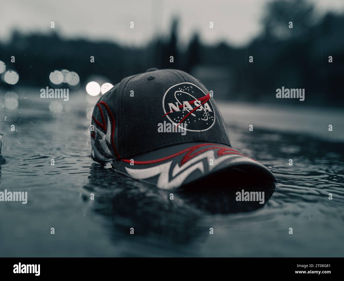 A baseball cap is pictured in a rain-filled pond, with city lights ...