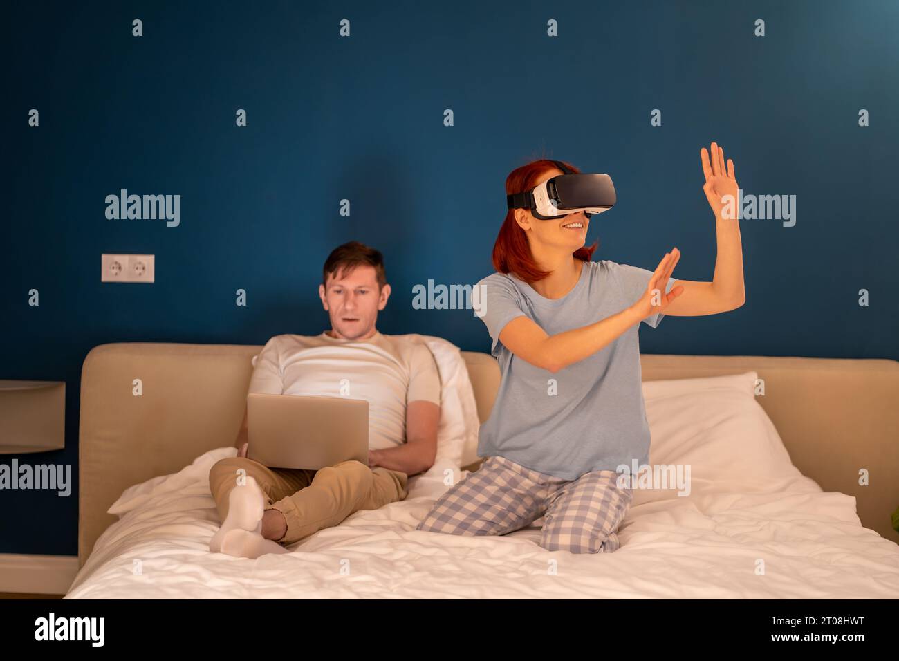 Interested woman in glasses virtual reality sits on bed with husband ...