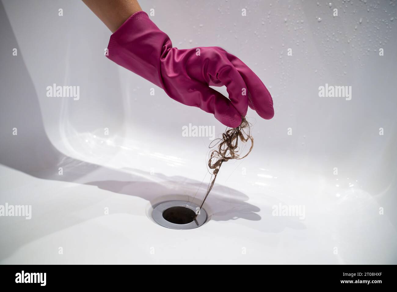 Hand of woman in pink rubber glove taking off hair clump from water ...