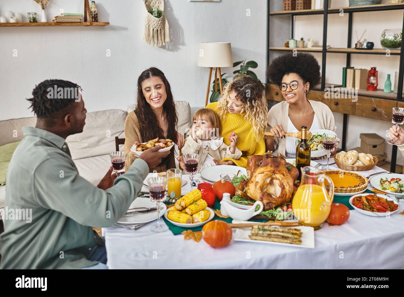 joyful multiethnic friends or family members sharing meal while ...