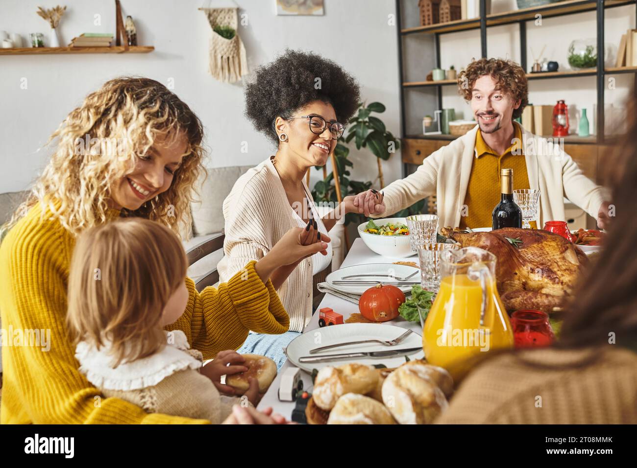 happy multiracial family holding hands and praying at Thanksgiving ...