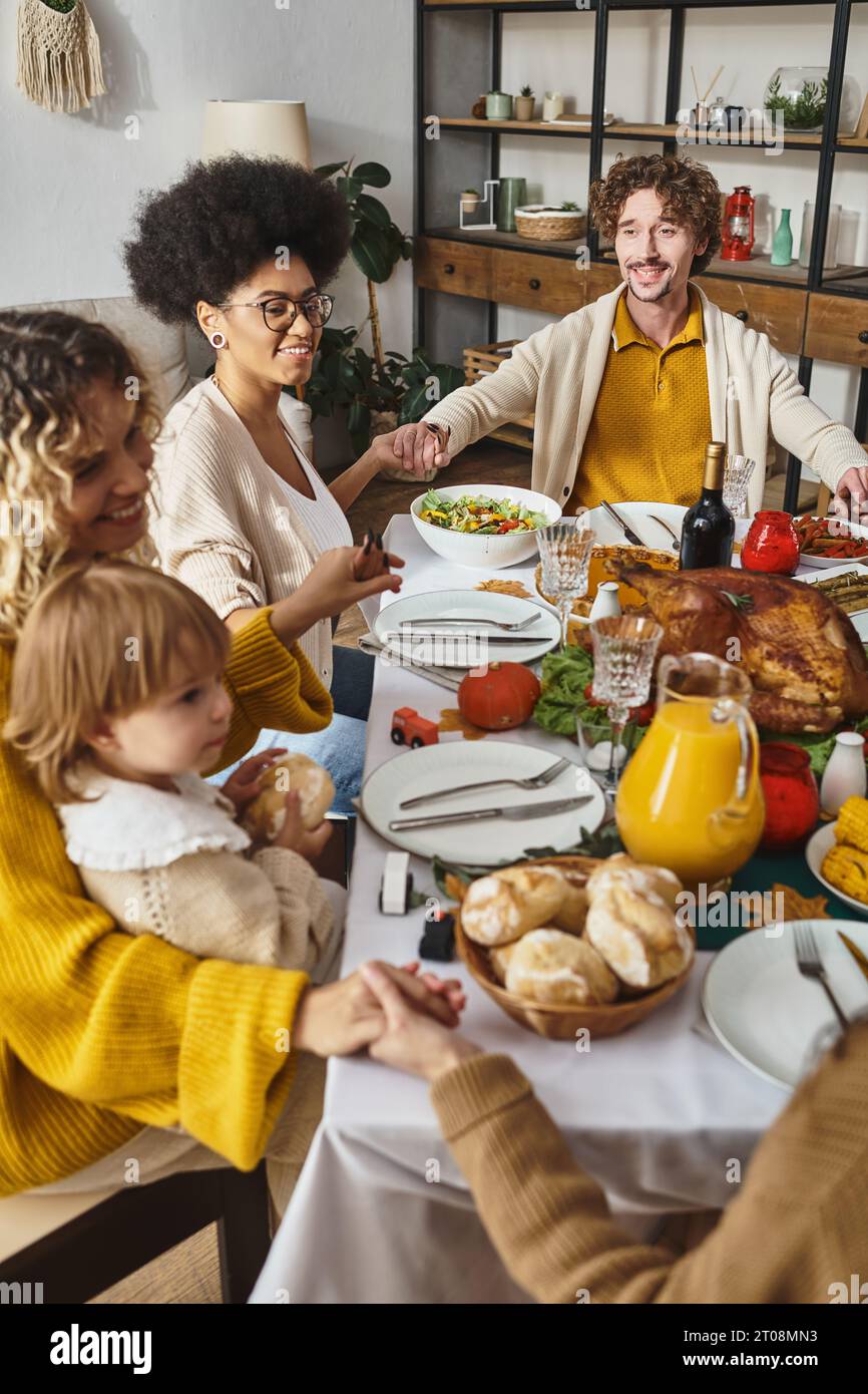 joyful multiracial family holding hands and praying at Thanksgiving ...