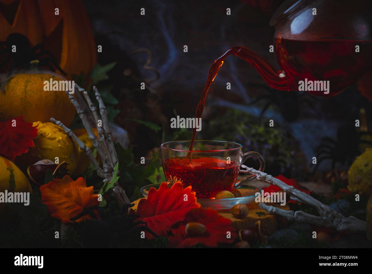 Pouring tea into glass cup surrounded by Halloween decorations, leaves ...