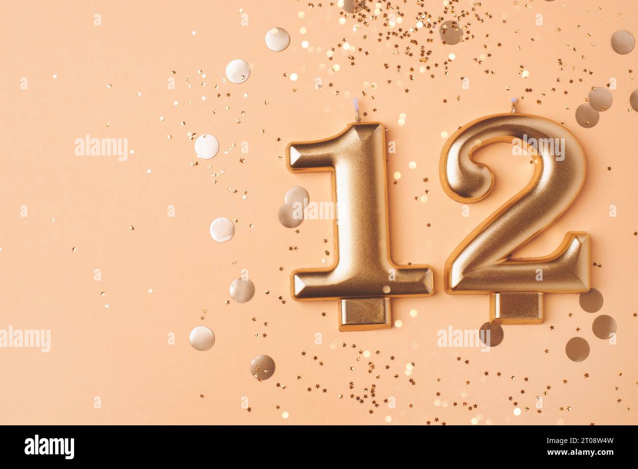 Gold candles in the form of number twelve on peach background with ...