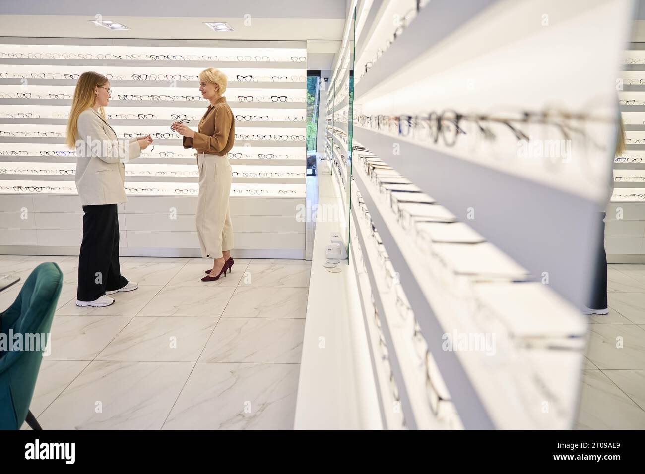 Client in elegant casual clothes tries on glasses in optical salon ...