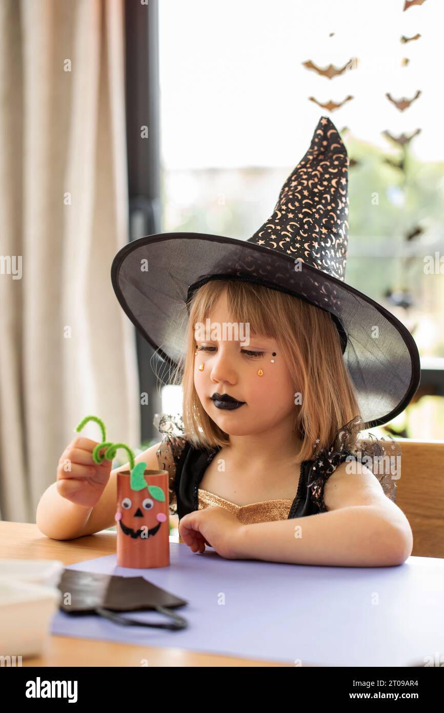 A cute girl in a witch costume makes a funny paper craft for Halloween ...