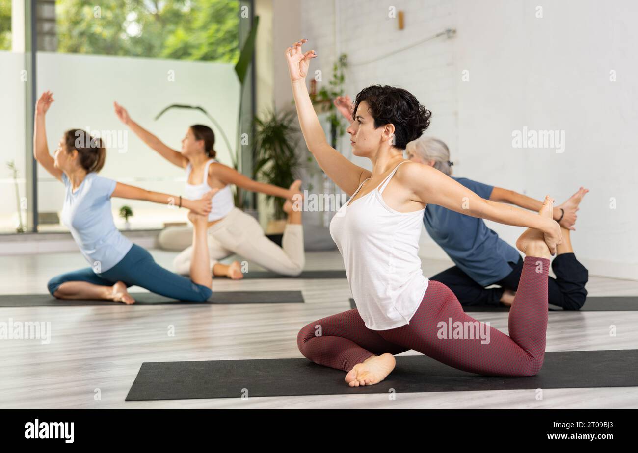 Group of active women practicing Dove pose Vajra Kapotasana yoga ...
