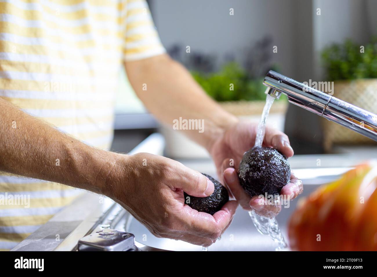 Side view of crop anonymous male washing avocado with water stream from ...