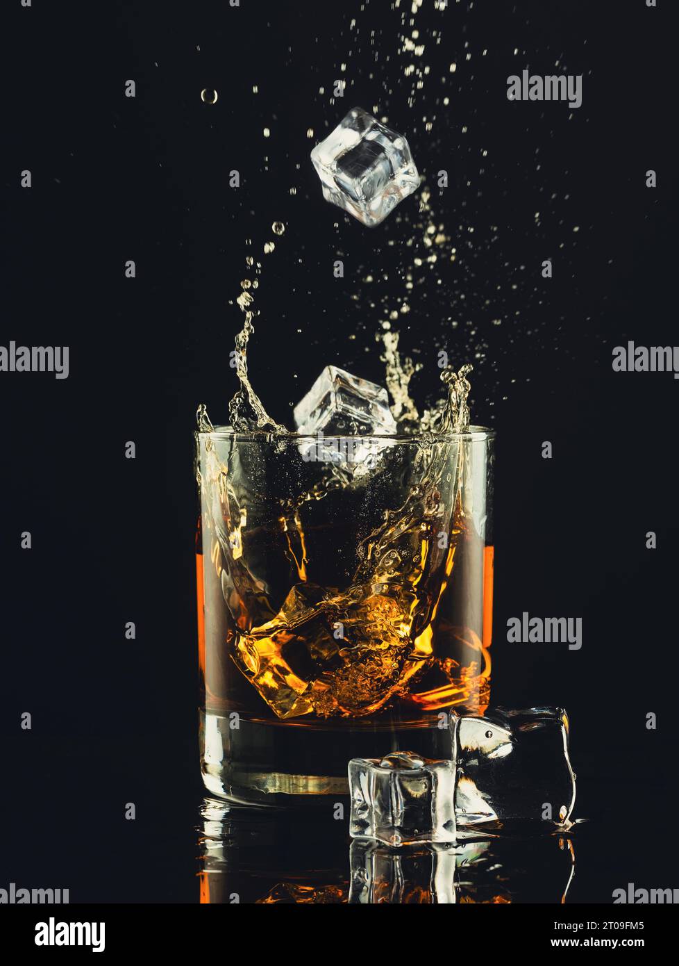 A glass of whisky, cognac or rum with 3 ice cube on black background making a big splash with ...
