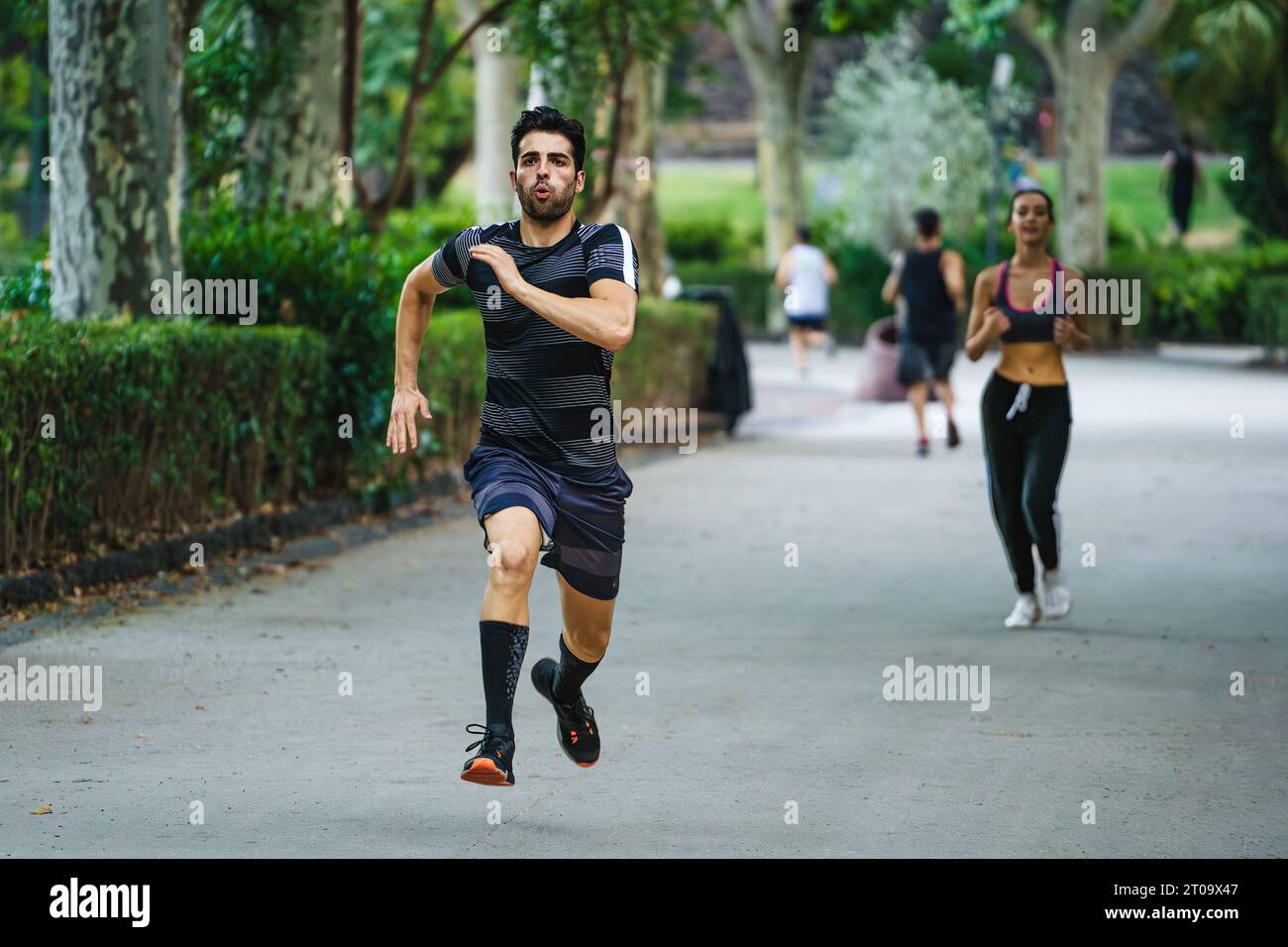 Young adult in sportswear jogging on a park path, with fellow runners ...