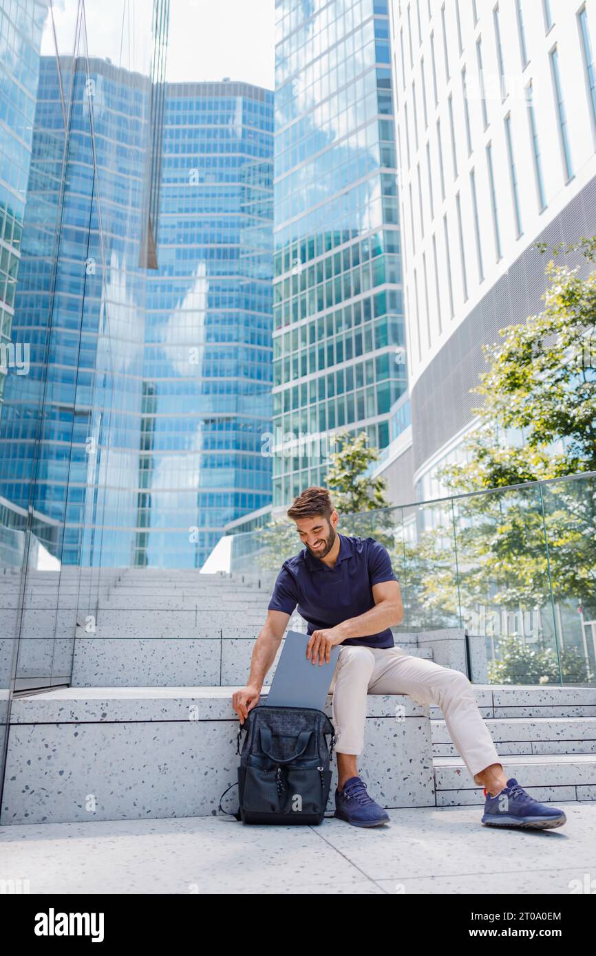 Male freelancer putting laptop inside backpack while sitting on steps ...