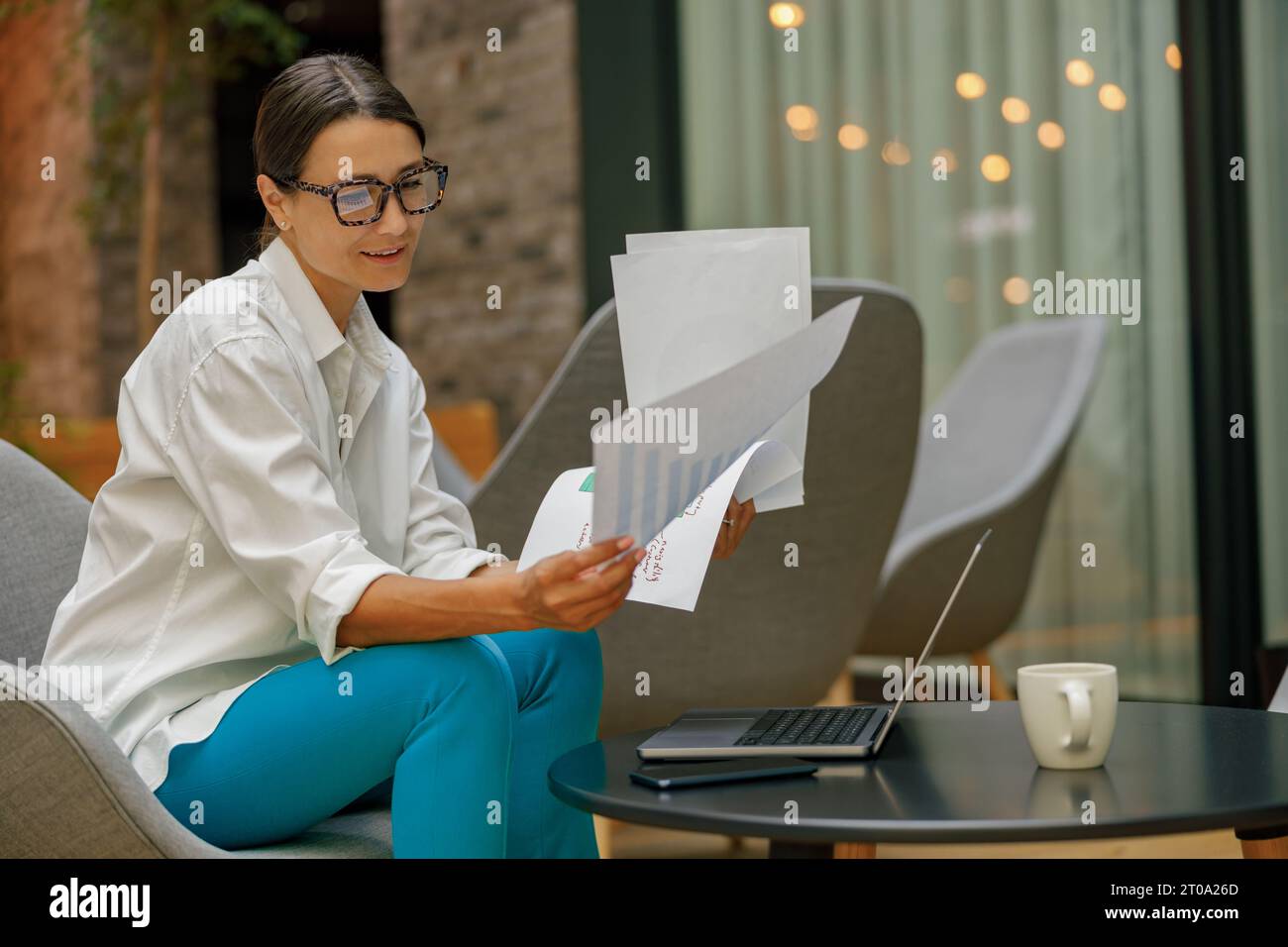 Pretty female entrepreneur working with documents and use laptop while ...