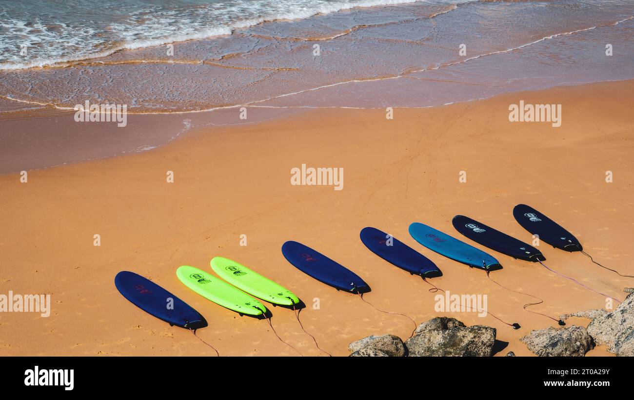 A line of blue and green surf boards on a beach with the sea in the ...