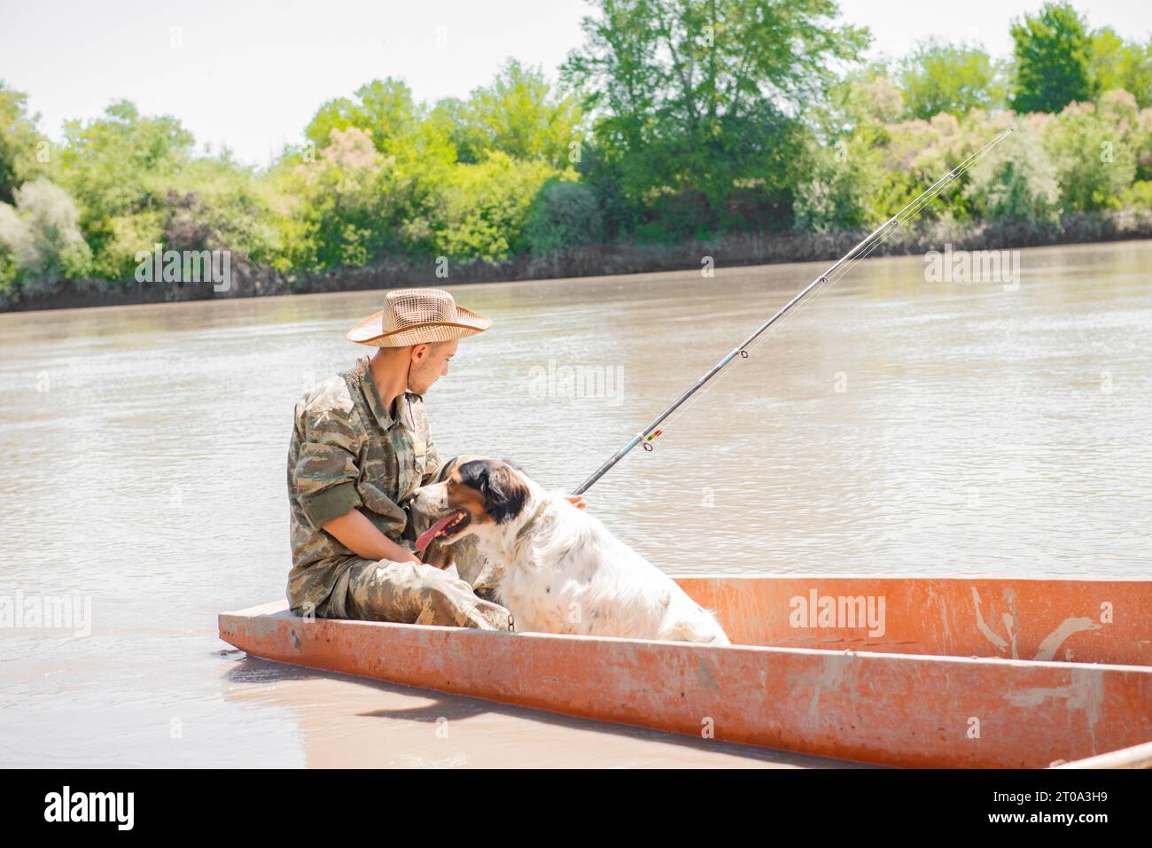 Thoughtful male angler with cute dog holding fishing rod, having rest ...