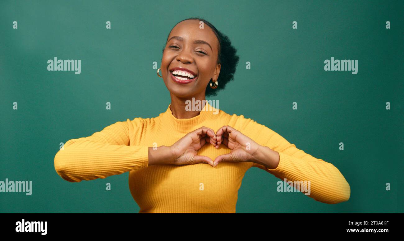 Young Black woman forms heart with hands to chest, smiling green studio ...