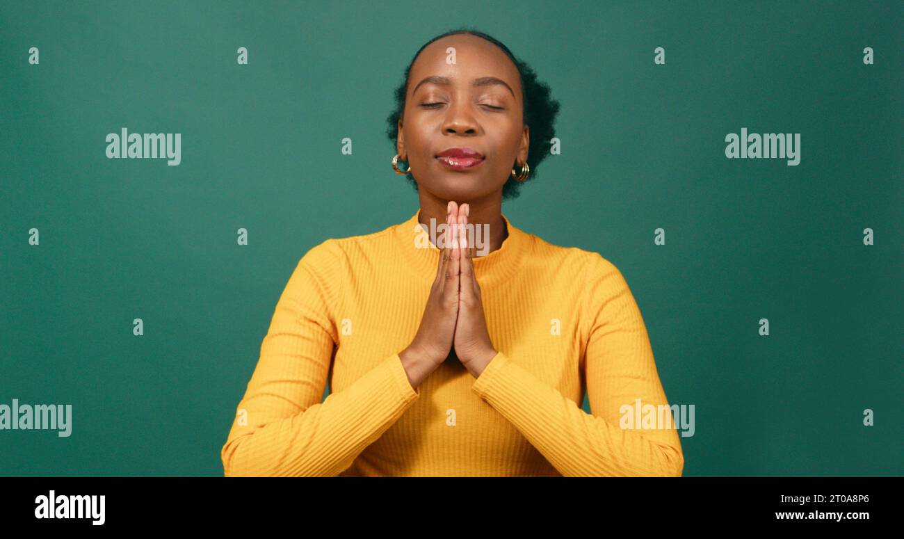 Calm young woman puts hands into prayer position, praying, green studio ...