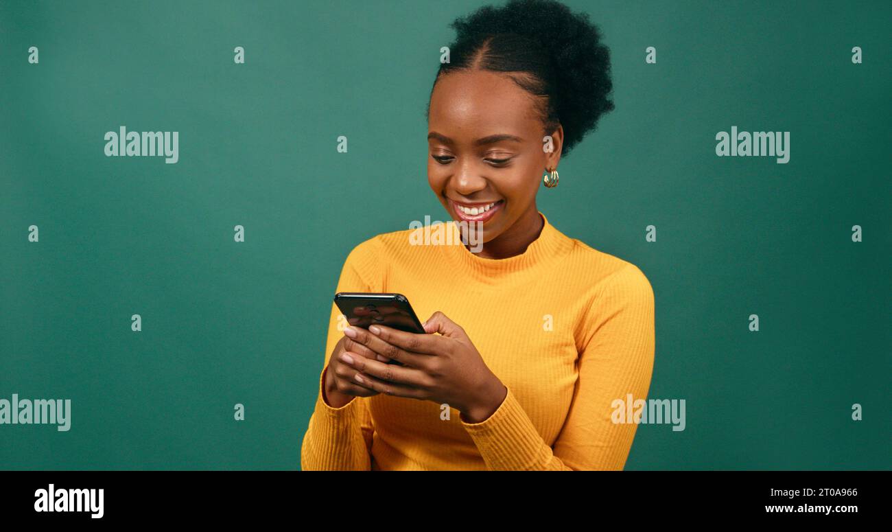Beautiful young woman texting on cellphone, smiling, green studio ...