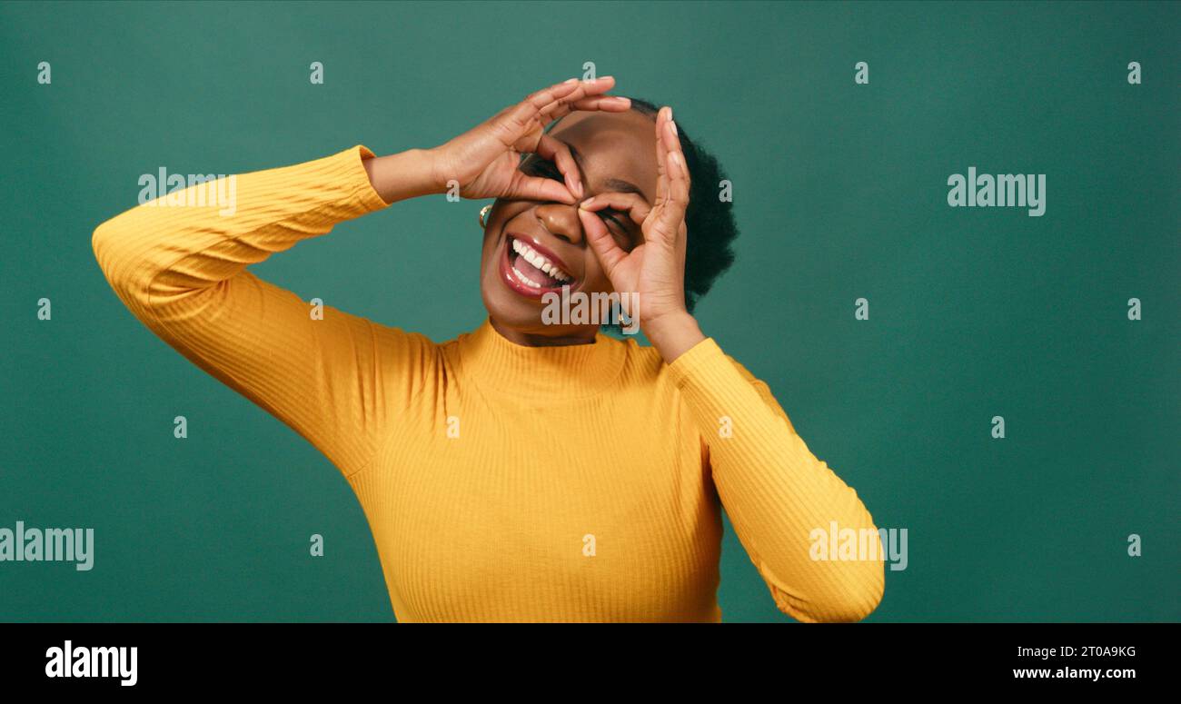 Beautiful Black woman pulls silly face with pretend eyeglasses, green ...