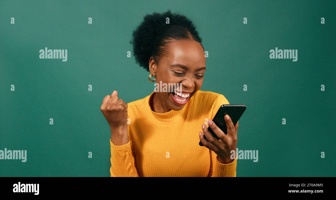 Young Black woman reads text message shocked excited, green studio ...