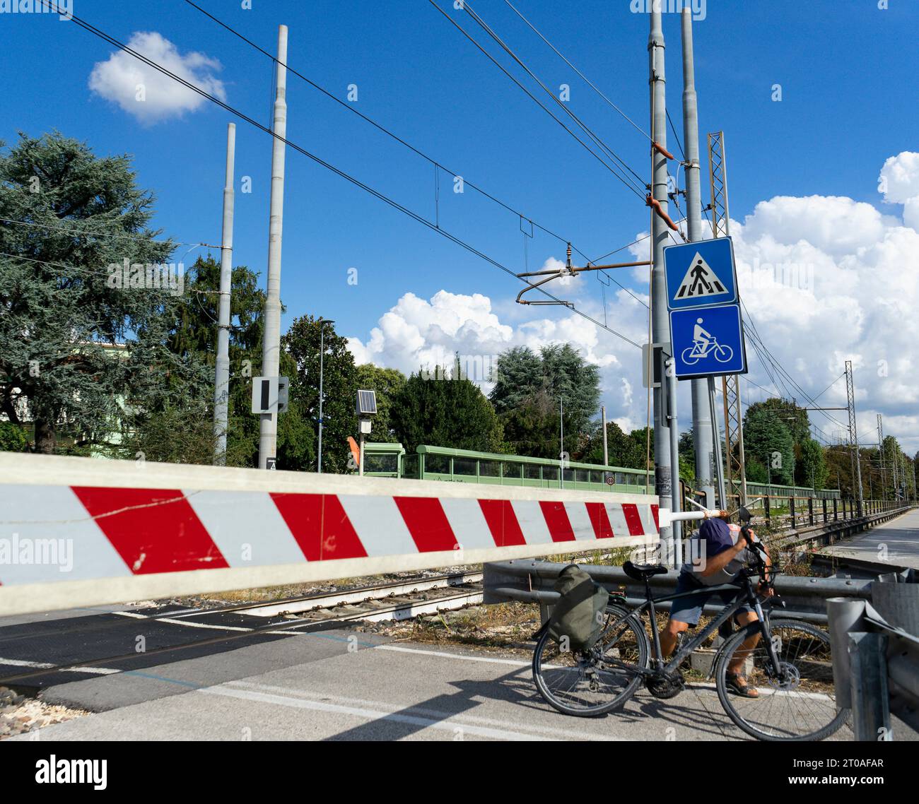 A man with a bicycle crosses the train tracks as the barrier prevents ...