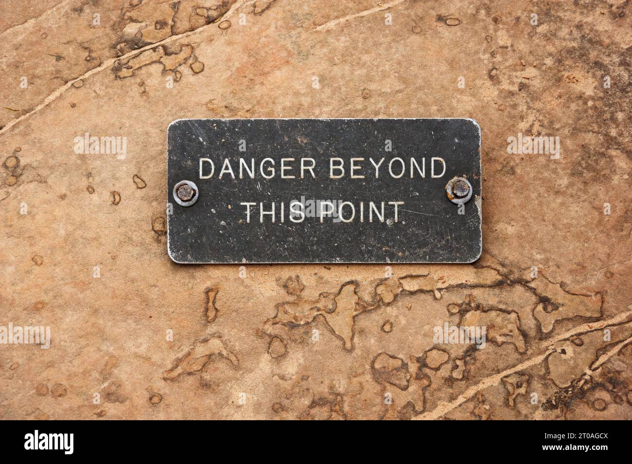 danger beyond this point sign bolted to sandstone rock warning of a ...