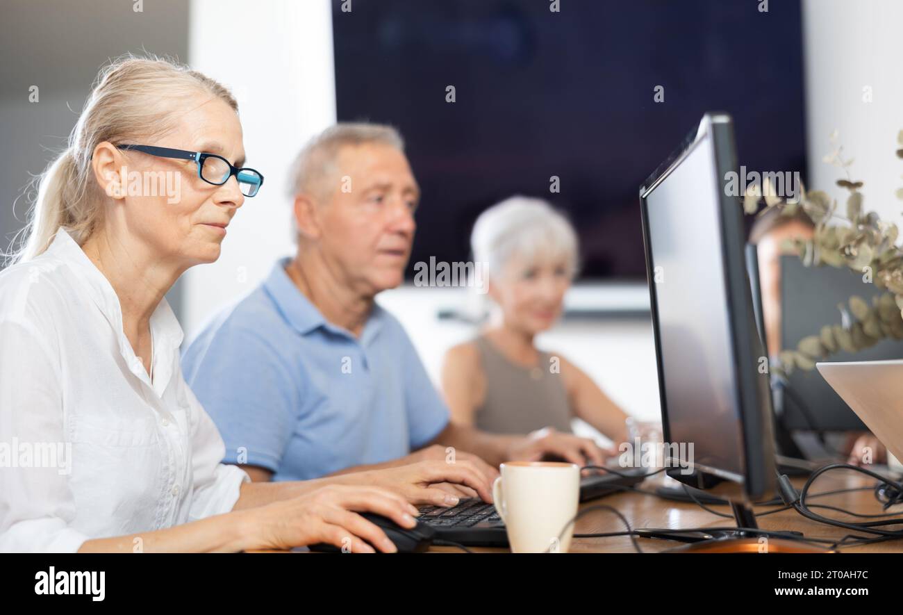 Concentrated elderly woman in glasses using computer during group ...