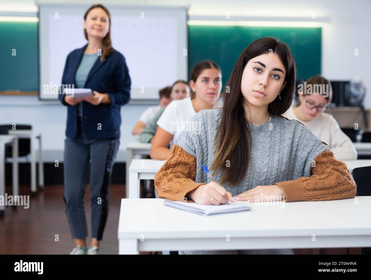 Group of school teenagers with pens and notebooks studying in classroom ...