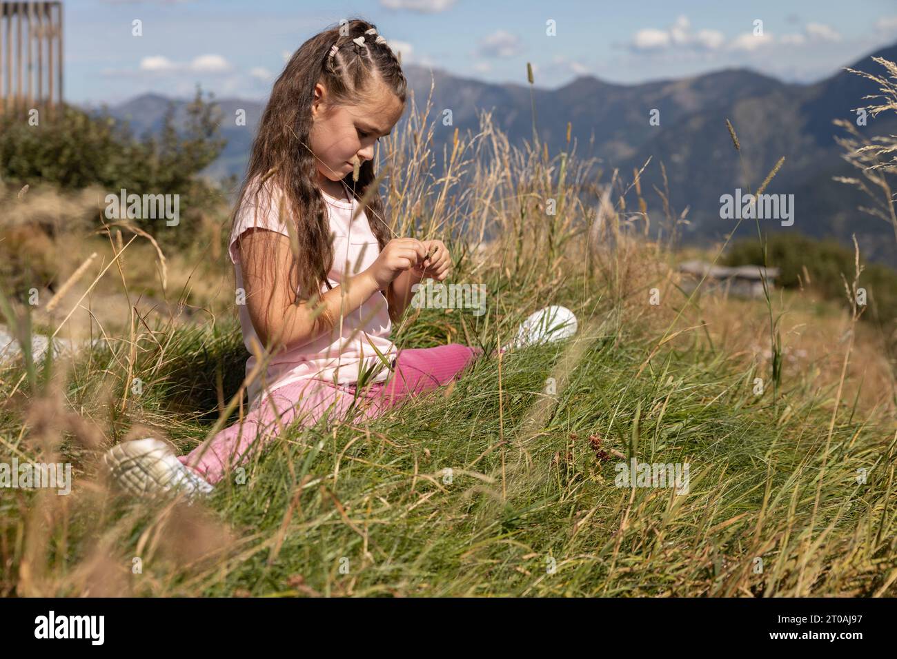 Cute little girl sitting in splits on grass playground in the mountains ...
