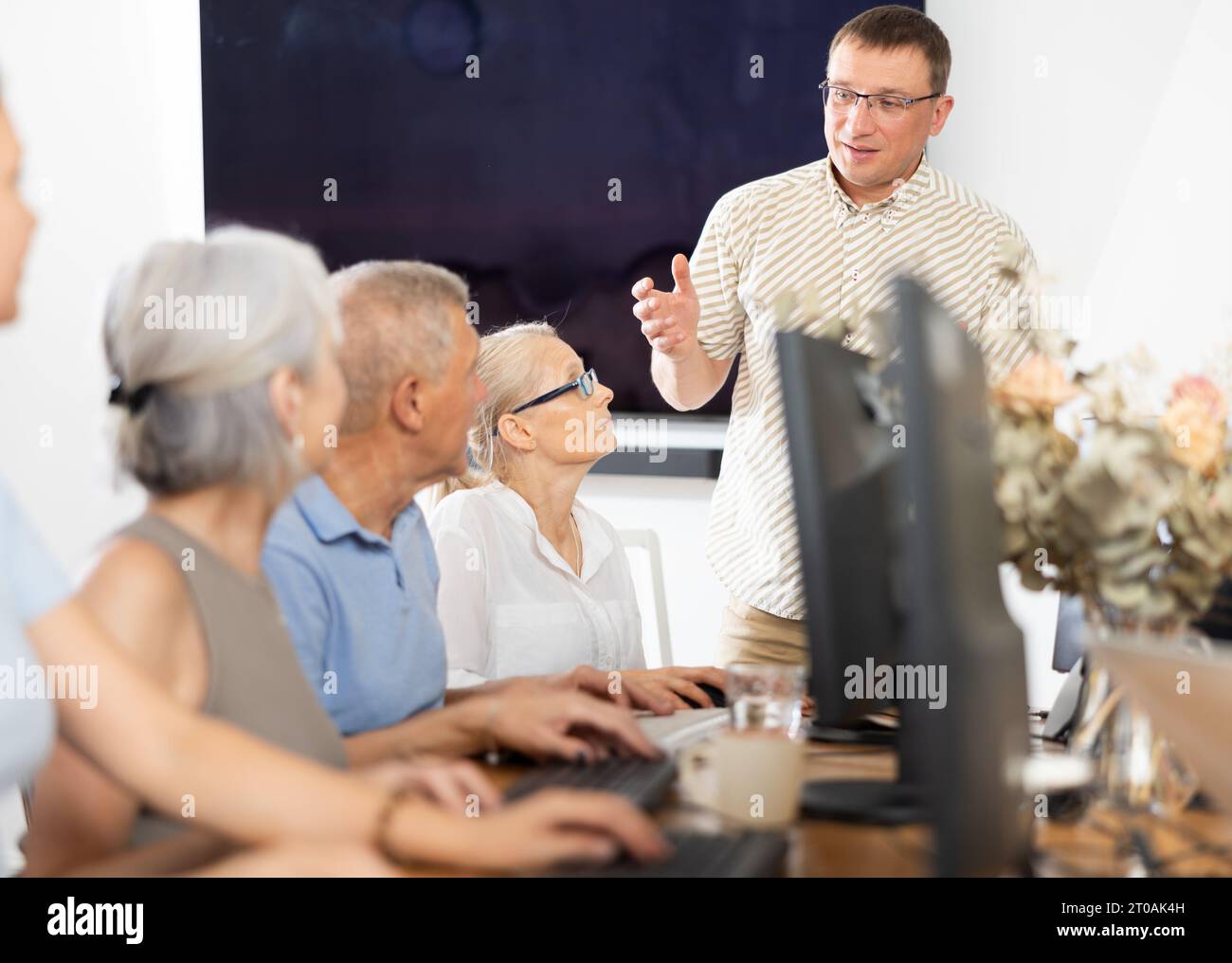 Male teacher teaching elderly people how to use computer Stock Photo ...