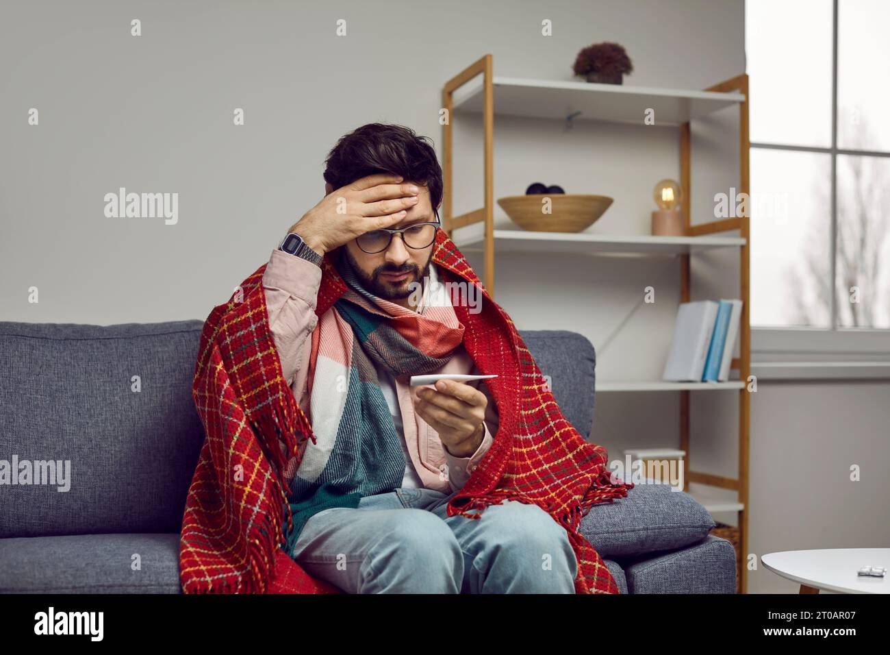 Sick man with fever looks confusedly at thermometer showing high body ...