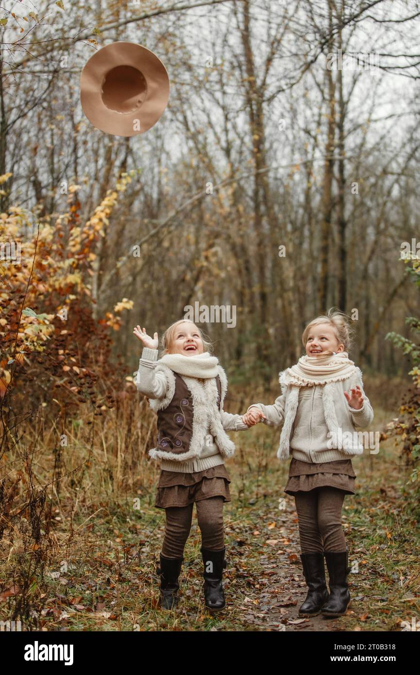 Twin girls play in the autumn park, throw their hats up. Horizontal ...
