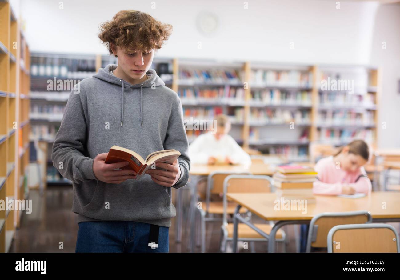 Teenager boy reading book in library Stock Photo - Alamy
