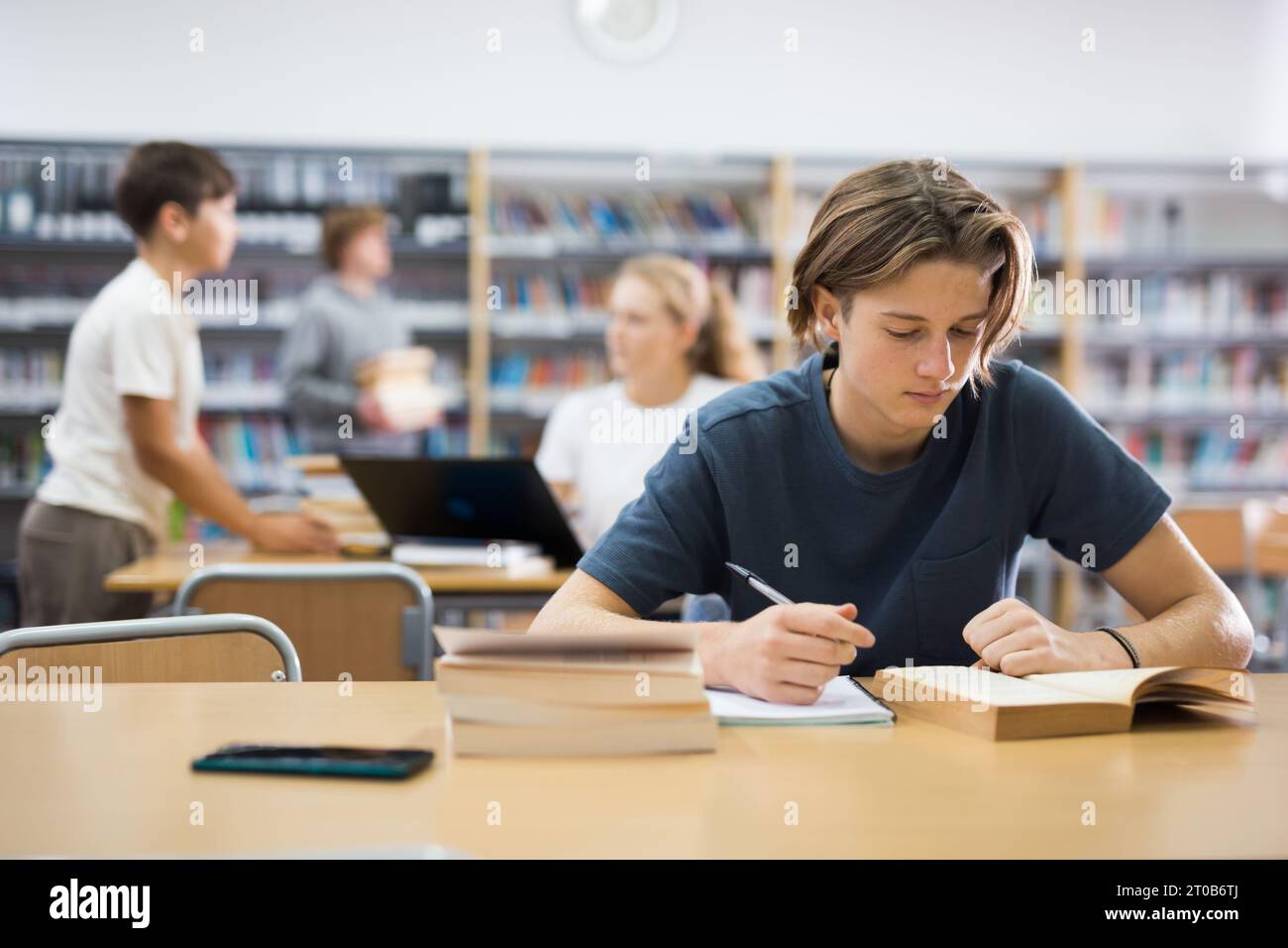Portrait of teenager reading books and writing in notebooks in library ...