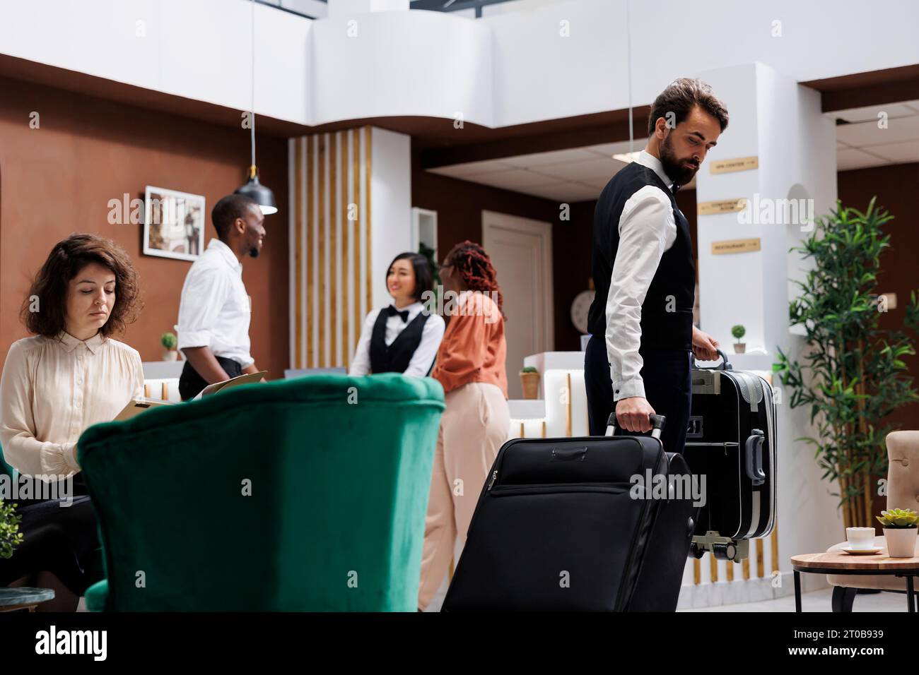 Male hotel porter carrying luggage to help people in reception lobby ...