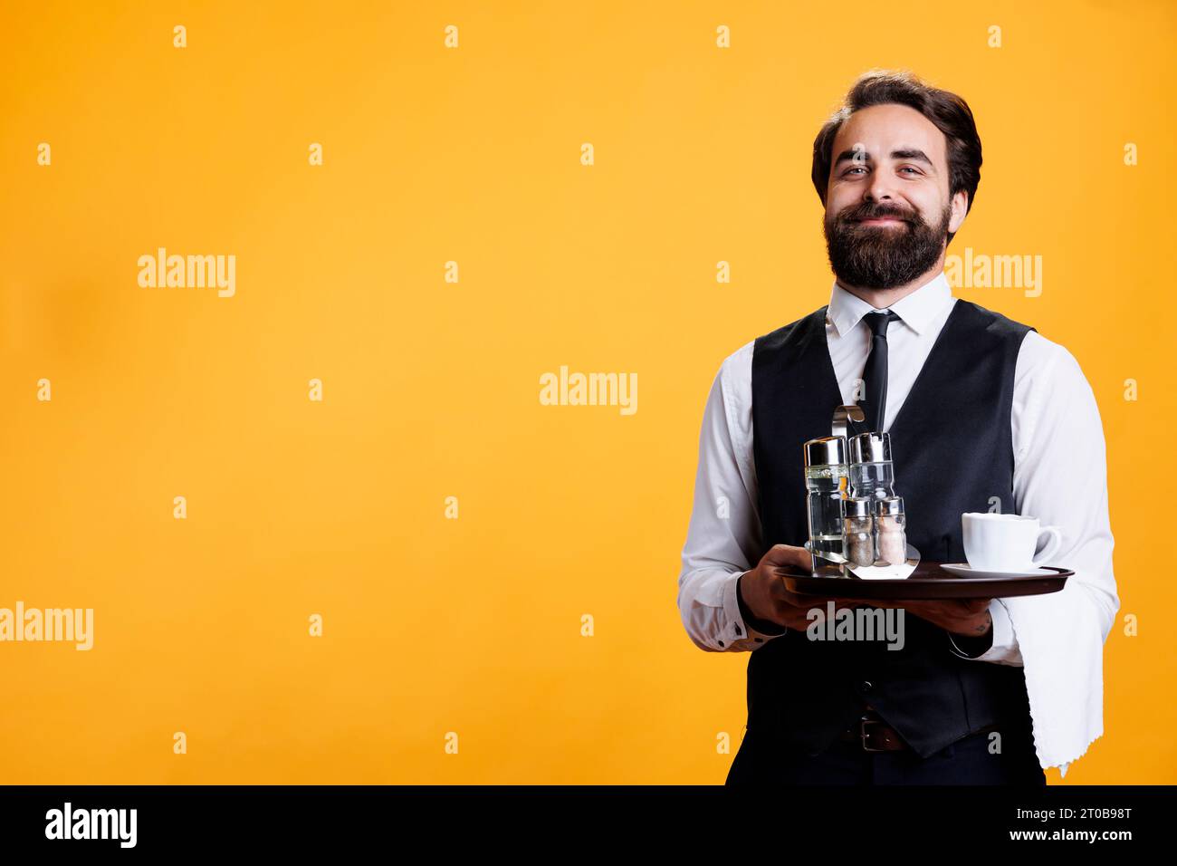 Smiling butler poses with platter in hand, standing against yellow ...