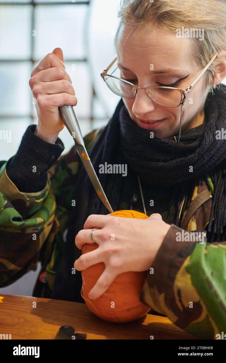 A modern blonde woman in military uniform is carving spooky pumpkins ...