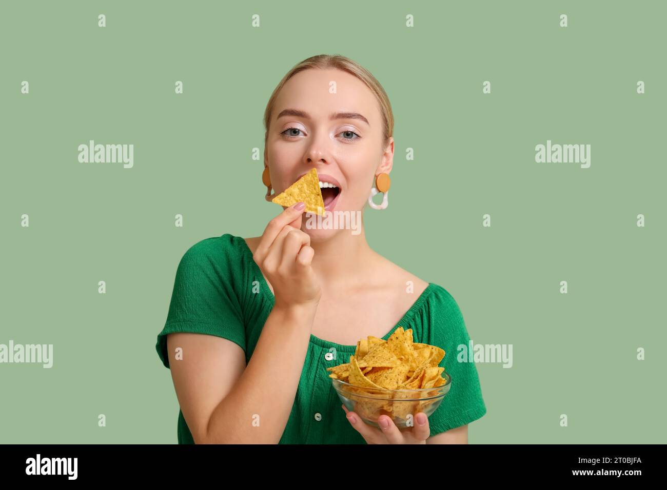 Pretty young woman eating nachos on green background Stock Photo - Alamy