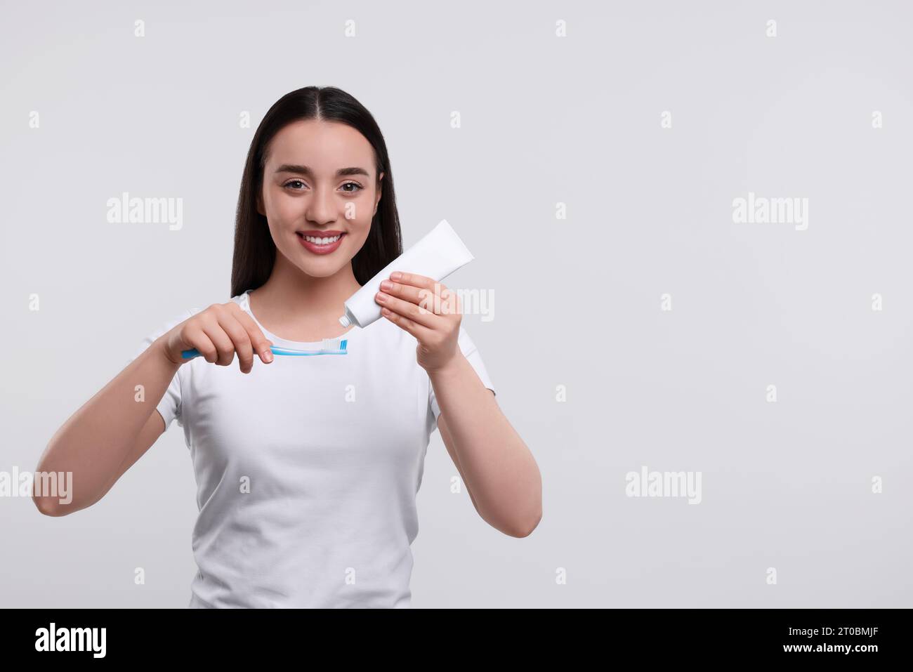 Happy young woman squeezing toothpaste from tube onto plastic ...