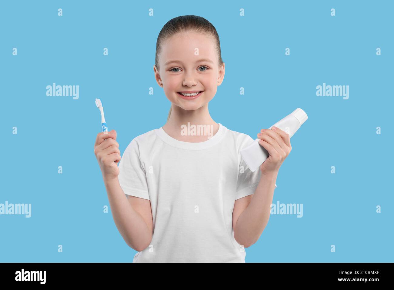 Happy girl holding toothbrush and tube of toothpaste on light blue ...