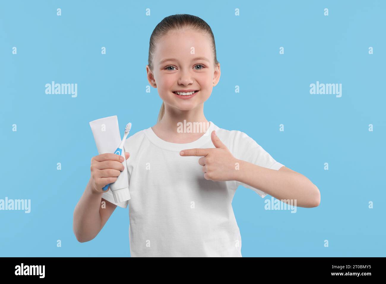 Happy girl holding toothbrush and tube of toothpaste on light blue ...