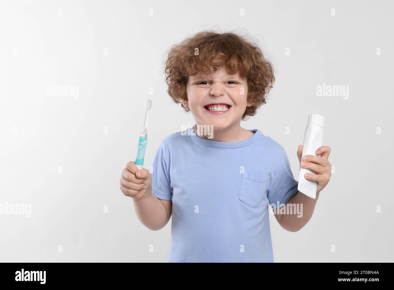 Cute little boy holding electric toothbrush and tube of toothpaste on ...