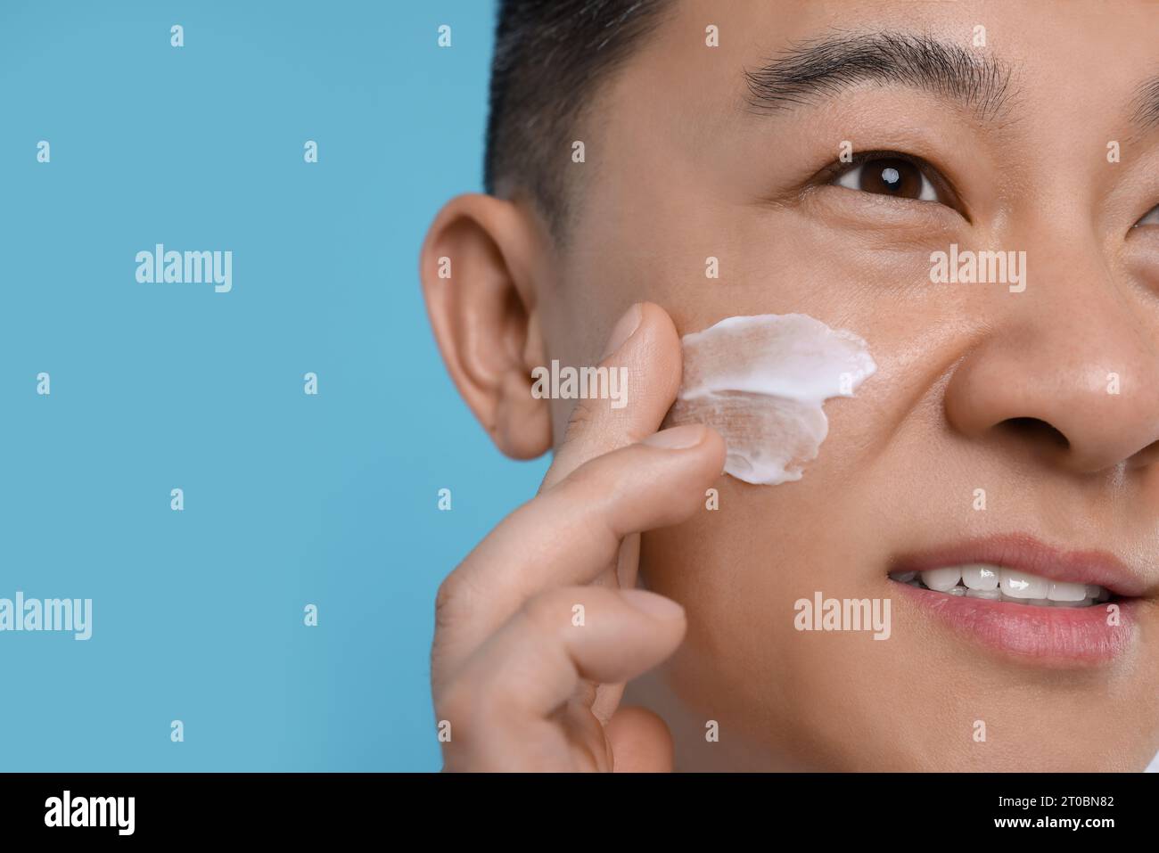 Man applying cream onto his face on light blue background, closeup ...