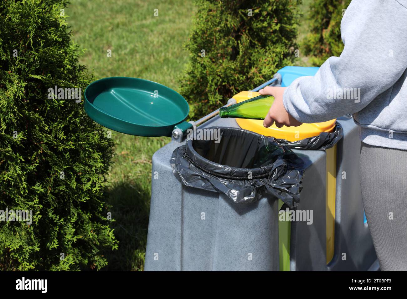Woman throwing glass bottle in bin outdoors, closeup. Recycling concept ...