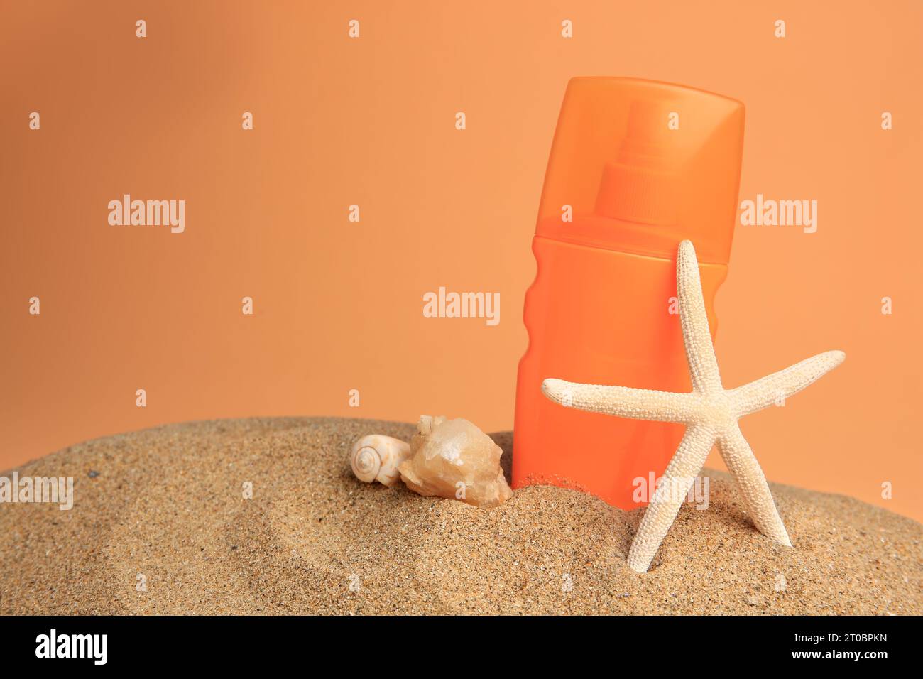 Sand with bottle of sunscreen, starfish and seashells against orange ...