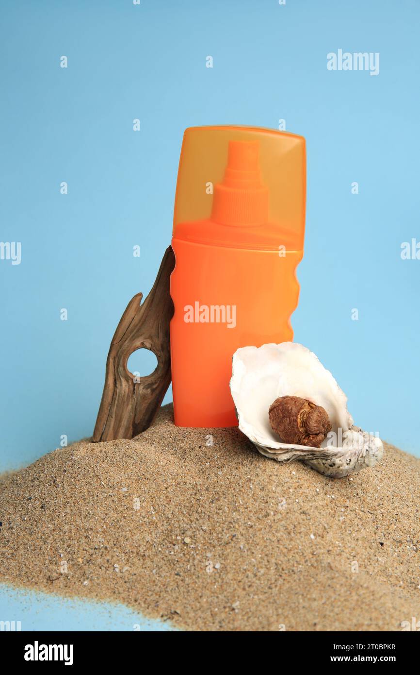 Sand with bottle of sunscreen, tree bark and seashells against light ...