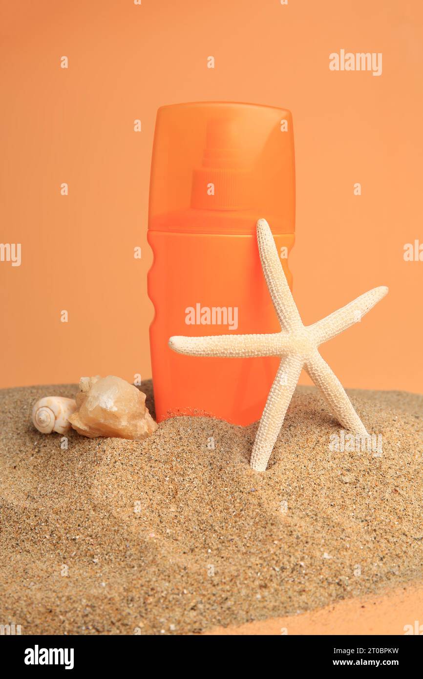 Sand with bottle of sunscreen, starfish and seashells against orange ...