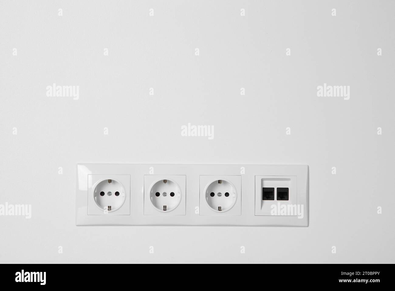 Many power sockets with ethernet plate on white wall indoors. Space for ...